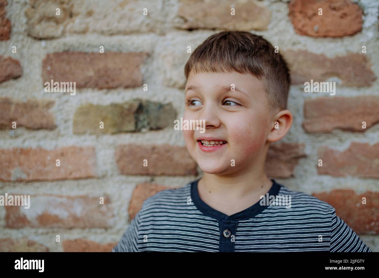 Little boy standing by brick wall and making funny faces in street ...