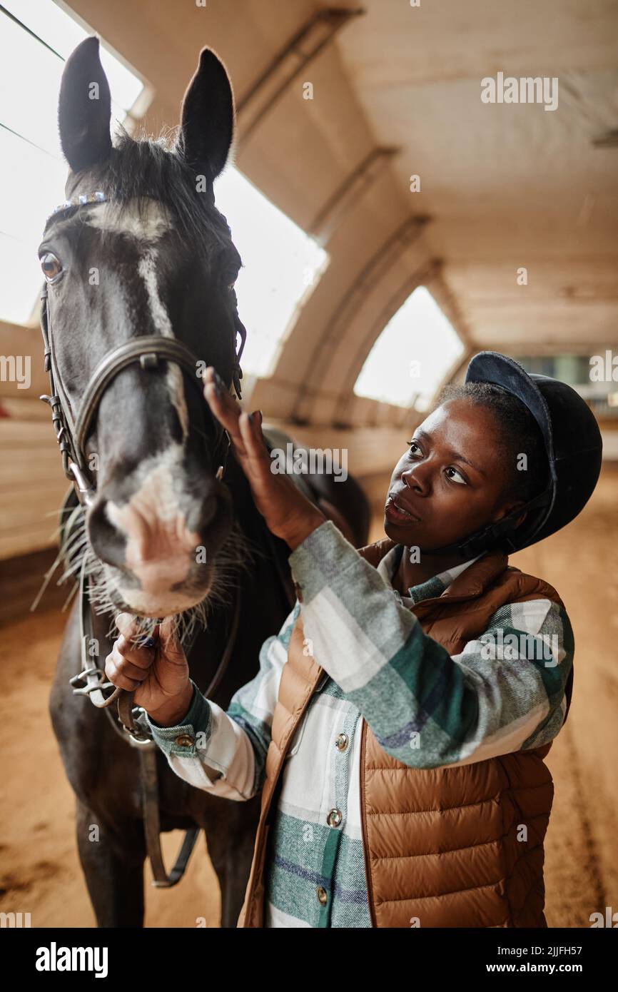 Vertical portrait of young black woman with horse in indoor riding ...