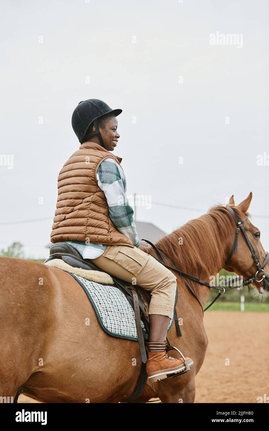 Vertical back view at young woman riding horse in ranch and wearing ...