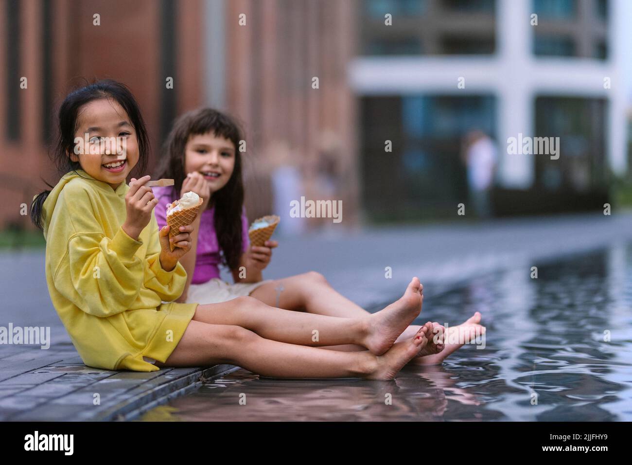 Two girls sitting, having legs in fountain, enjoying ice cream and ...