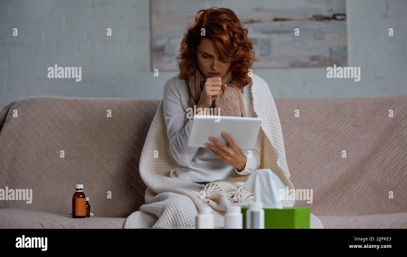 redhead sick woman using digital tablet and coughing near medication ...