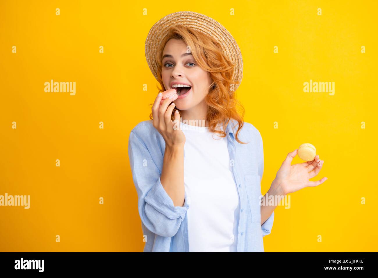 Woman eating a macaroon. Beautiful redhead woman in summer straw hat ...