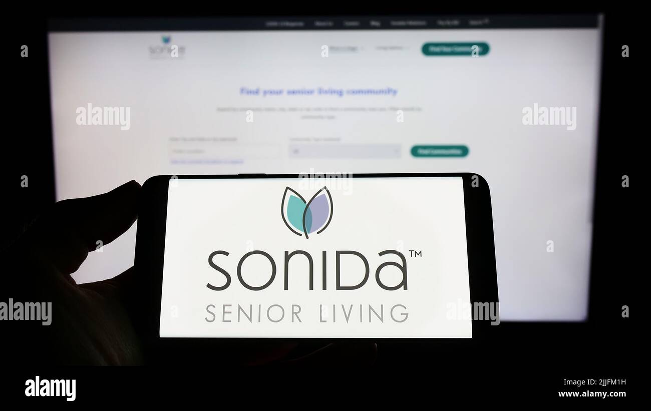 Person holding mobile phone with logo of American company Sonida Senior ... Person holding mobile phone with logo of American company Sonida Senior ...