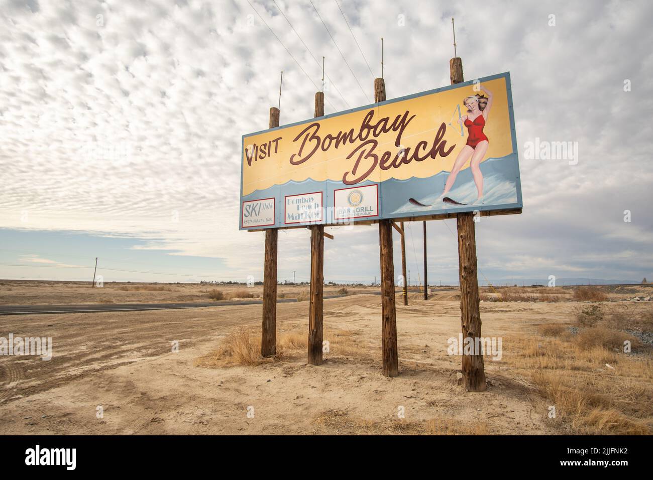 A Vintage billboard that says visit Bombay Beach by a road in cloudy ...