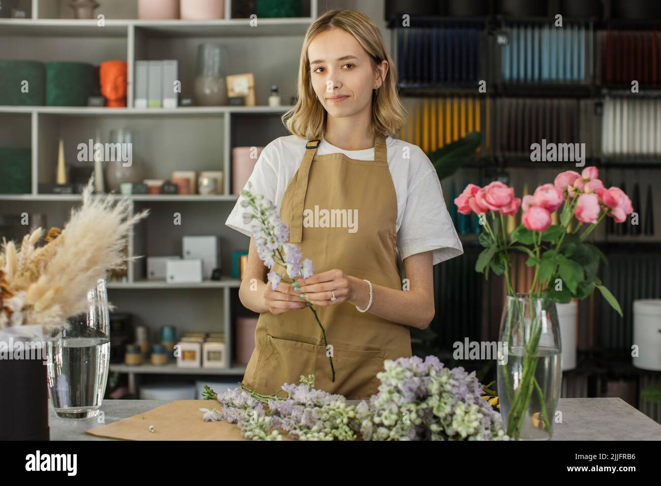 Portrait of young female florist holding violet flowers and looking at ...