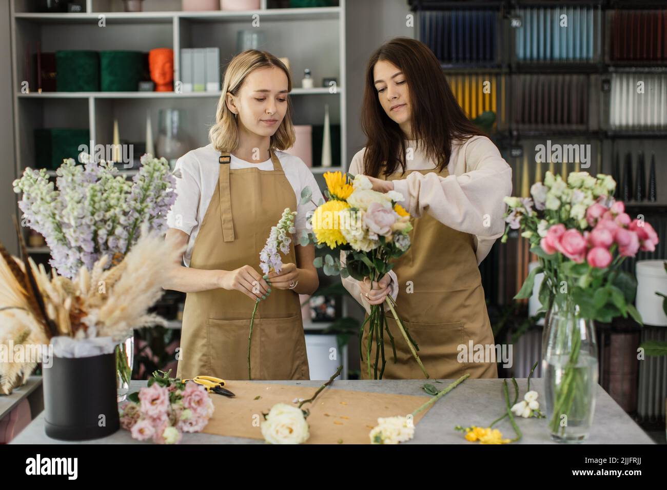 Concentrated female colleagues in aprons working together in flower ...