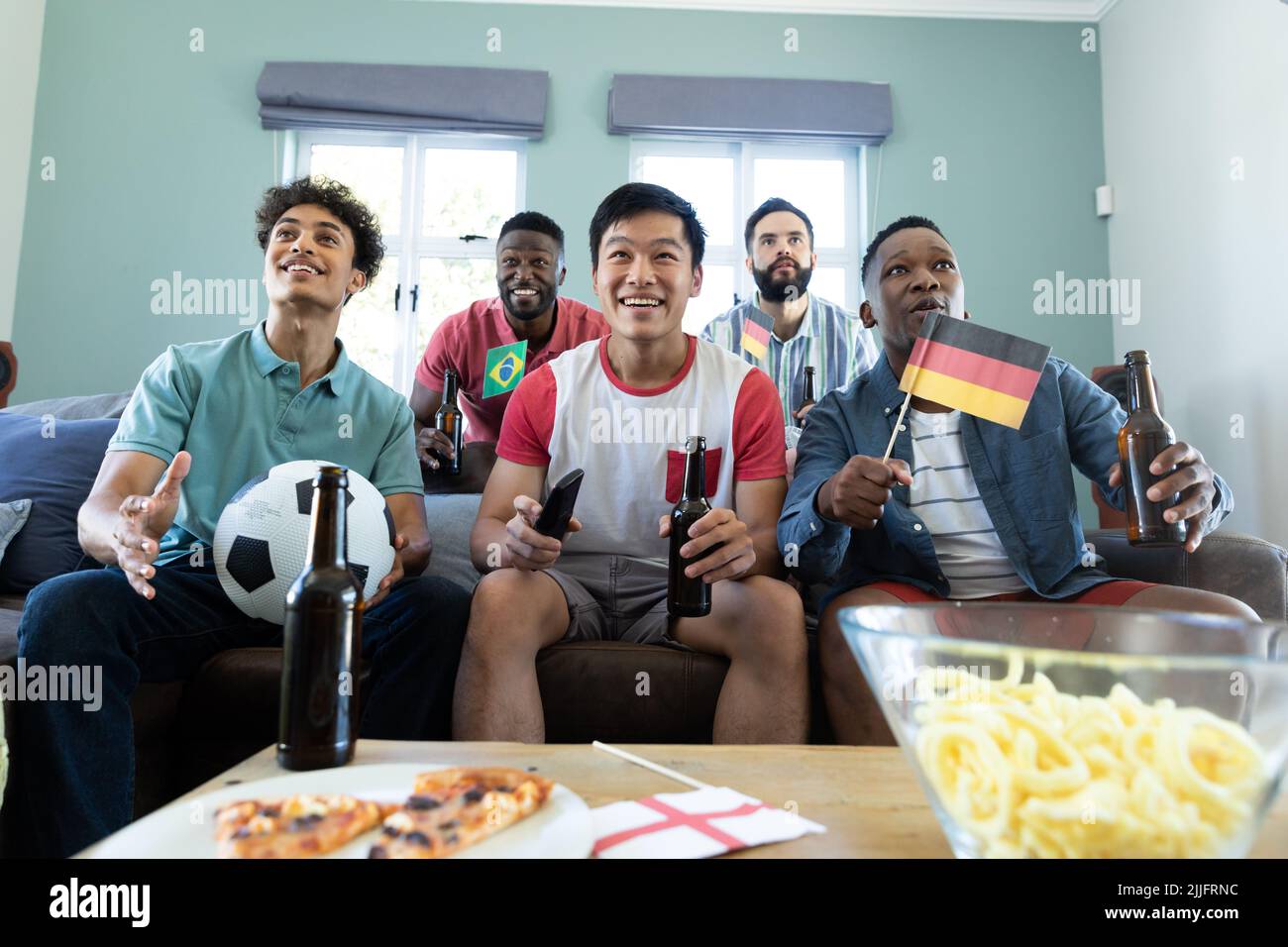 Multiracial curious male friends with beer bottles, flags and ball ...