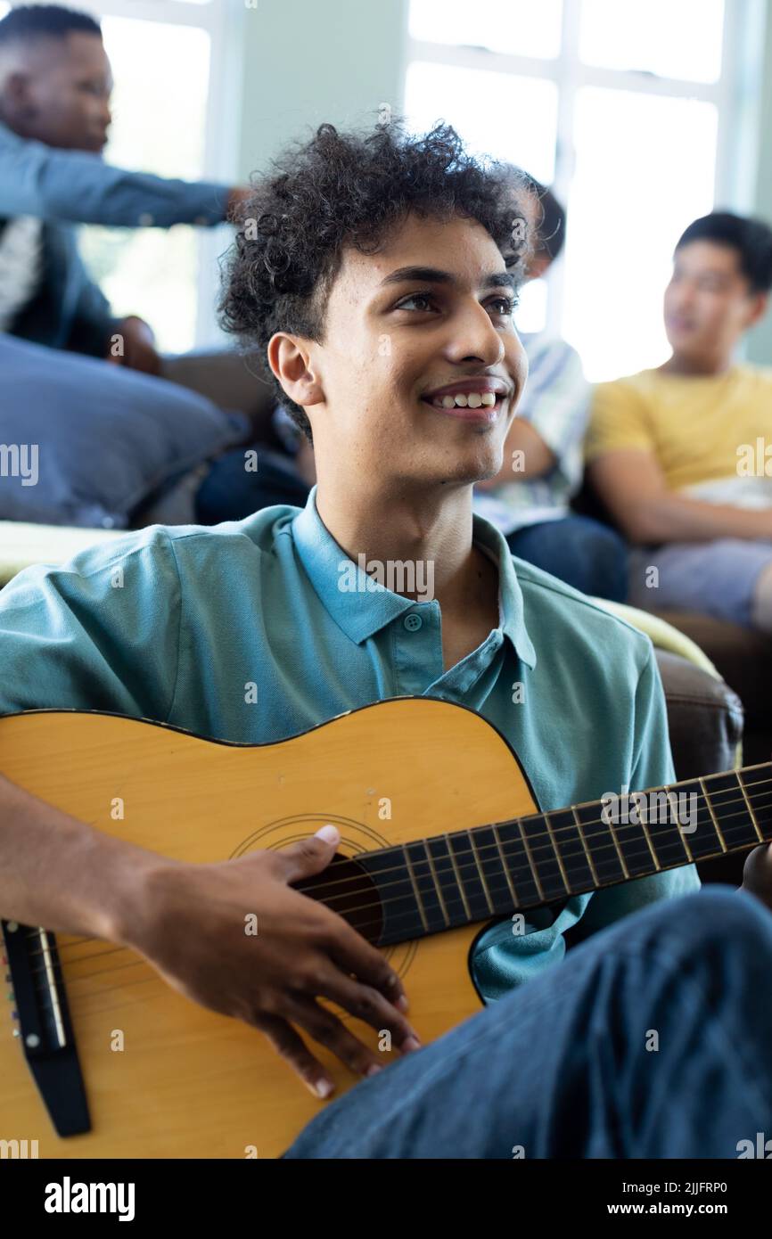 Smiling young man playing guitar while multiracial male friends ...