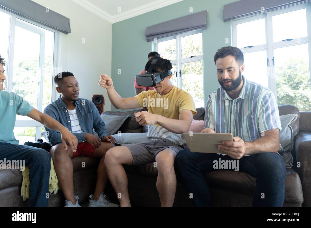 Multiracial man wearing virtual reality simulator gesturing and friend ...