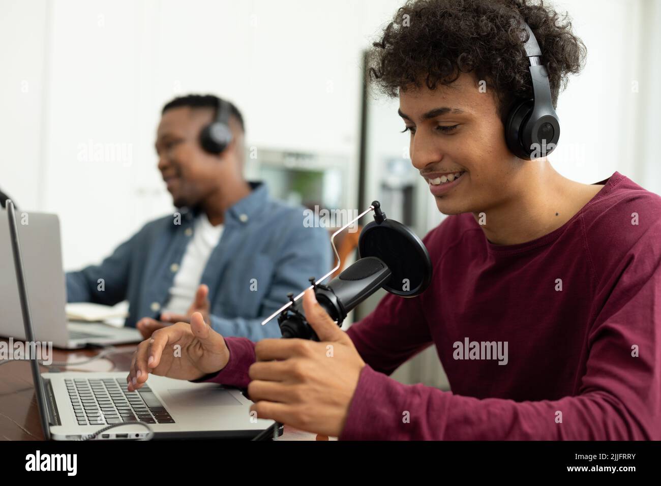 Smiling multiracial male podcaster speaking over microphone while ...