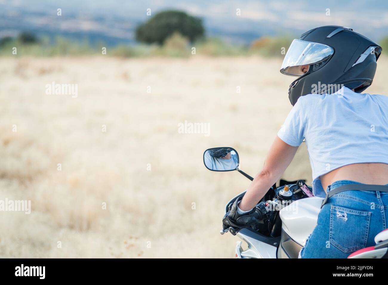 young biker woman from behind with blue t-shirt and safety helmet ...