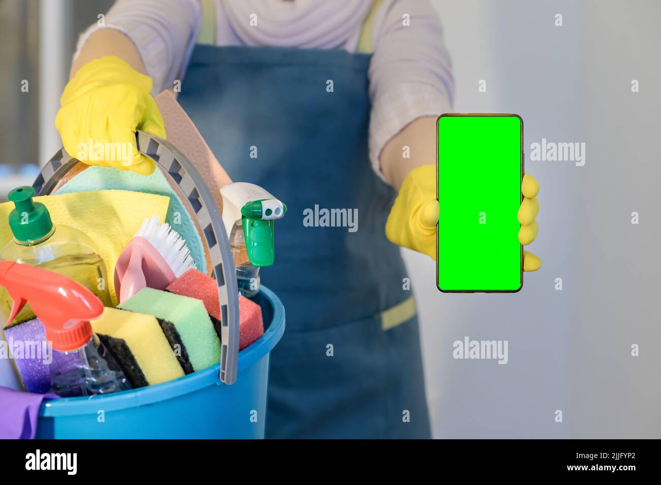 homeowner in rubber gloves holding detergent bottles. Hold mobile phone ...