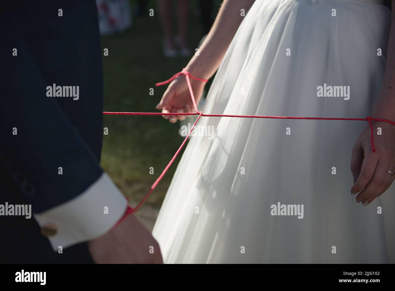 A closeup shot of a bride and groom with their hands tied with red ...