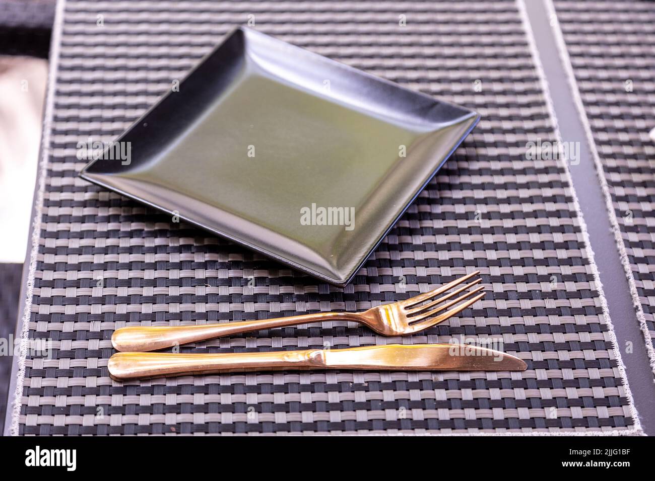 An empty black plate with a metal fork and knife on a vinyl mesh fabric ...