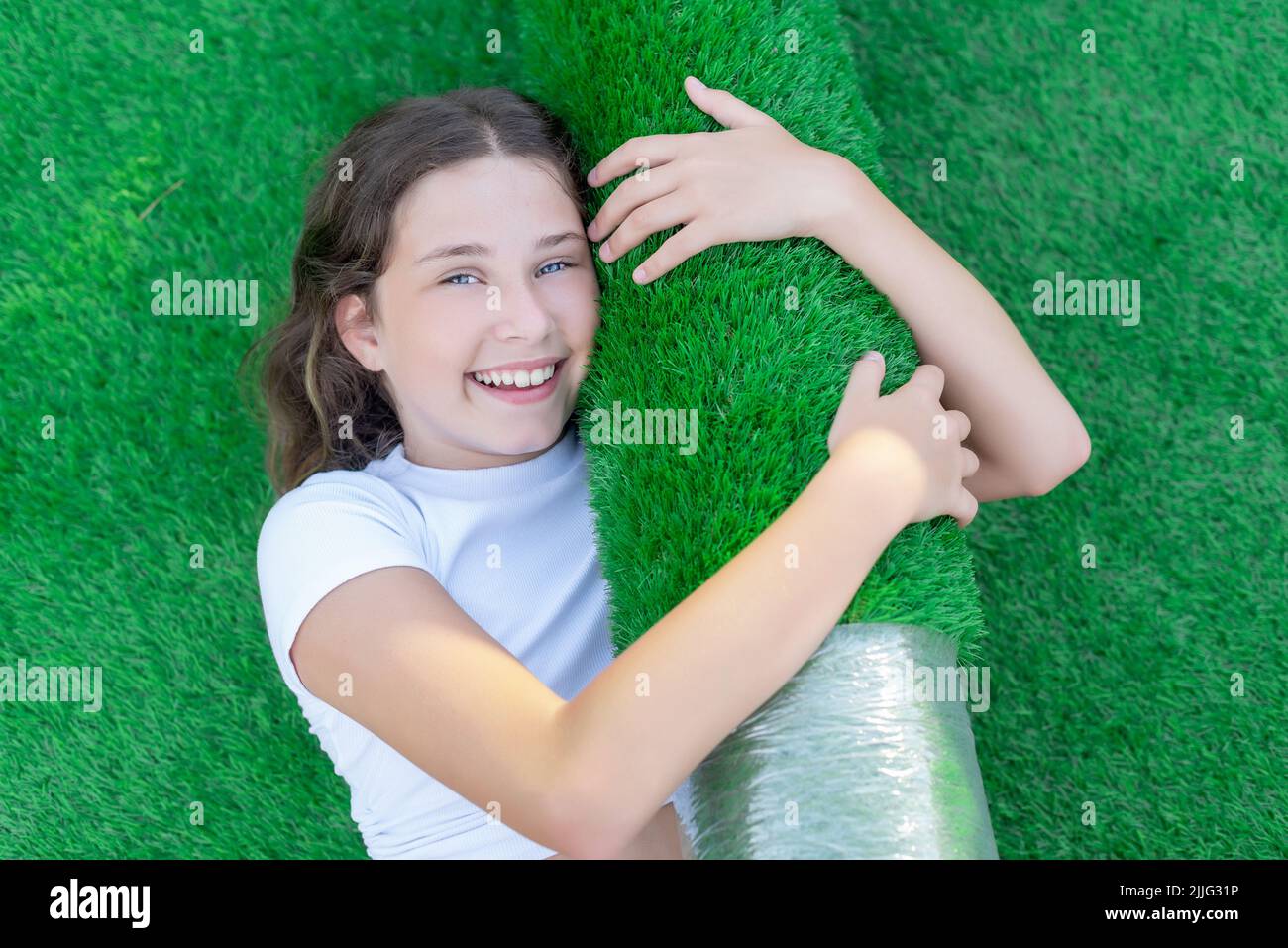 Smiling young caucasian girl lying on the lawn and hugging a new roll ...