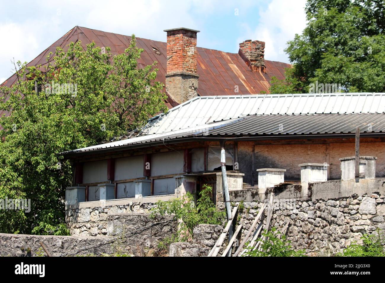 Devastated abandoned old traditional stone suburban family house with rusted metal sheet covered ...