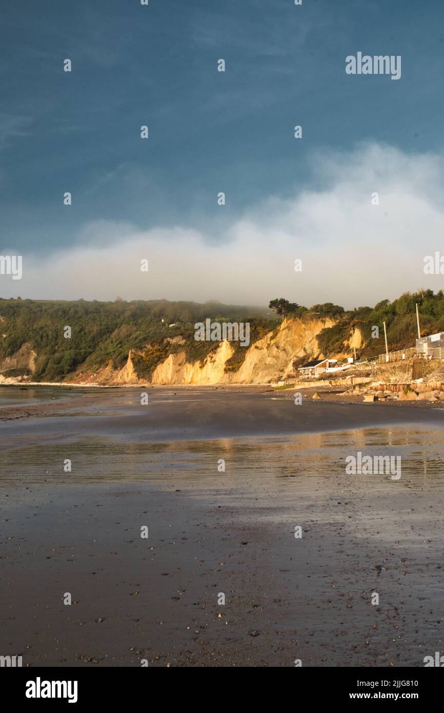A vertical shot of hills near the beach with fog coming from behind ...