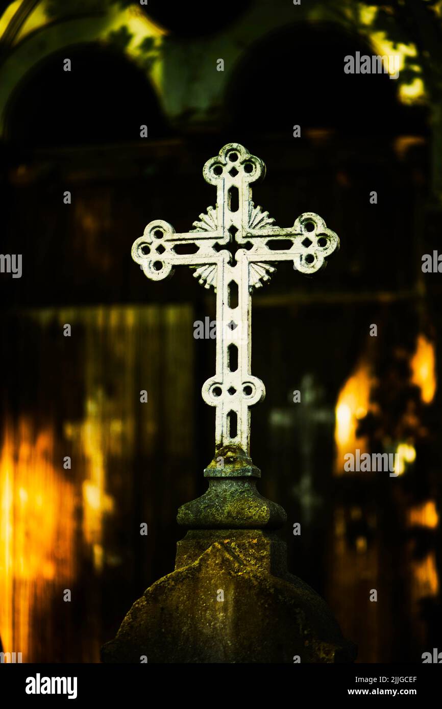A white old Christian cross stands on a stone pedestal in the shade of ...