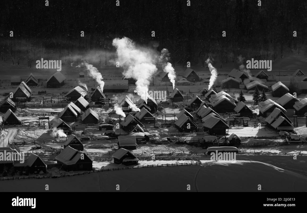 A grayscale view of village with small houses in winter. Smoke coming ...