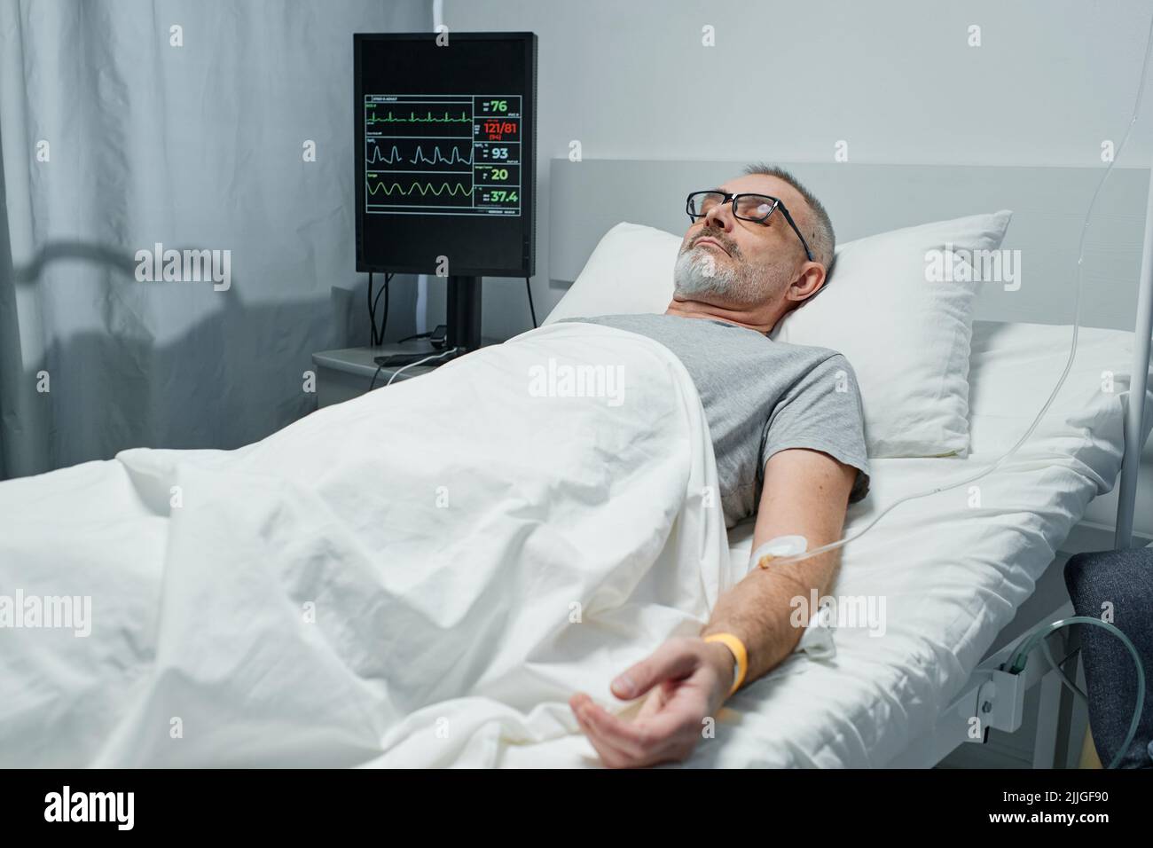 Mature Caucasian man wearing eyeglasses lying in bed in emergency room ...