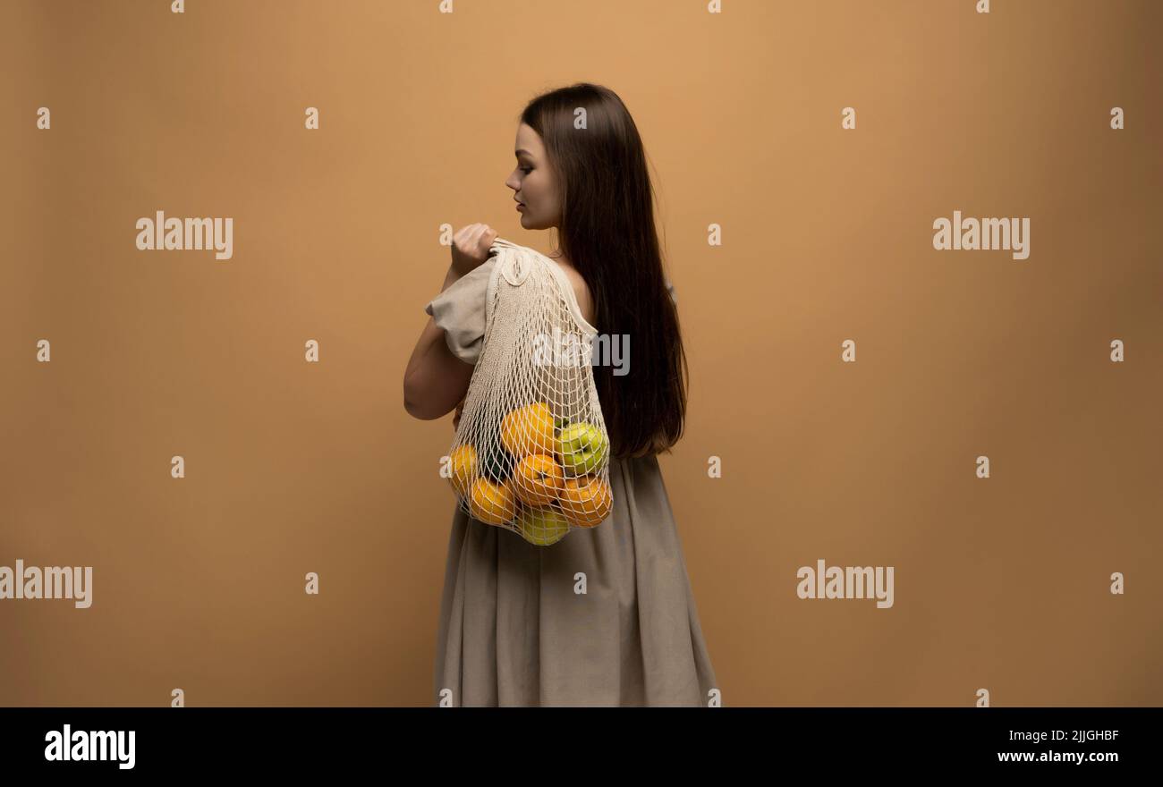 Back of woman in beige dress holding string shopping reusable mesh bag ...