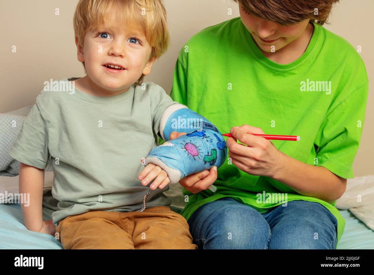 Brother boy draw with felt-tip pen on a broken hand cast to show ...