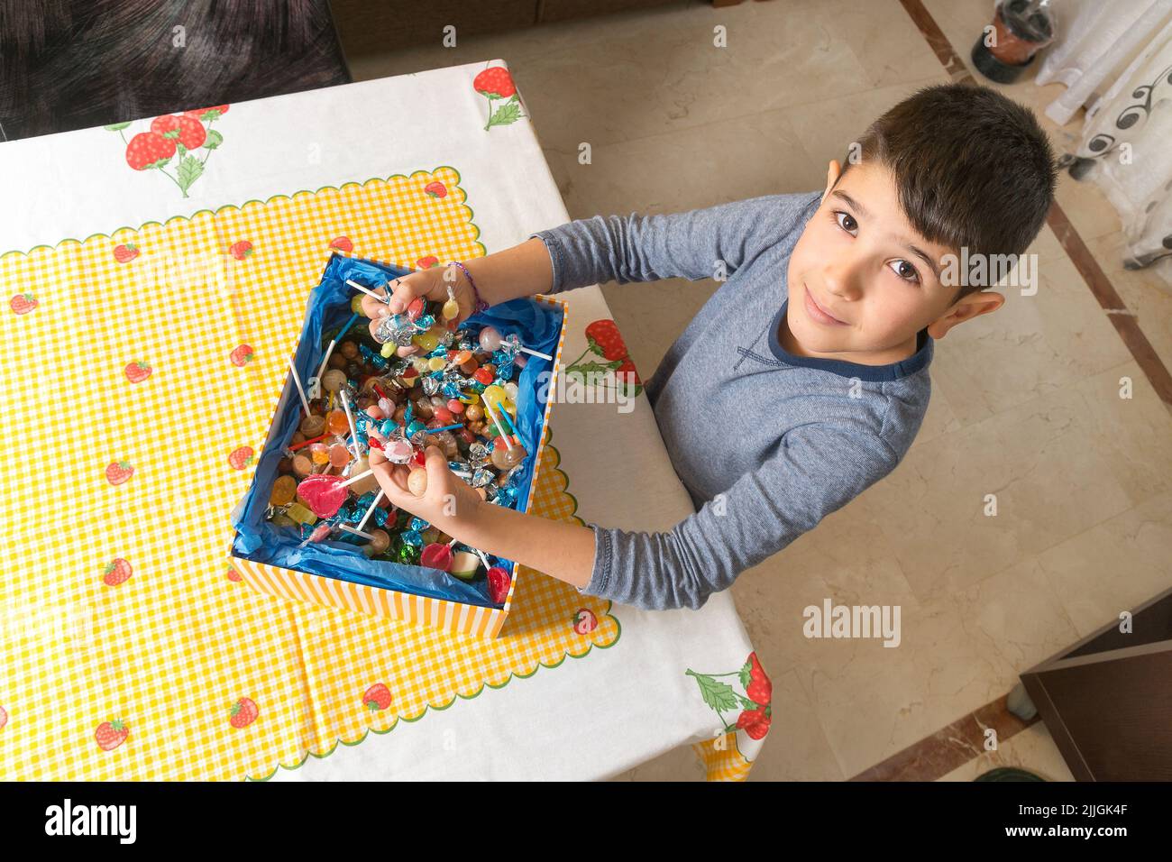 A Caucasian boy looks at the camera showing the handfuls of sweets he ...