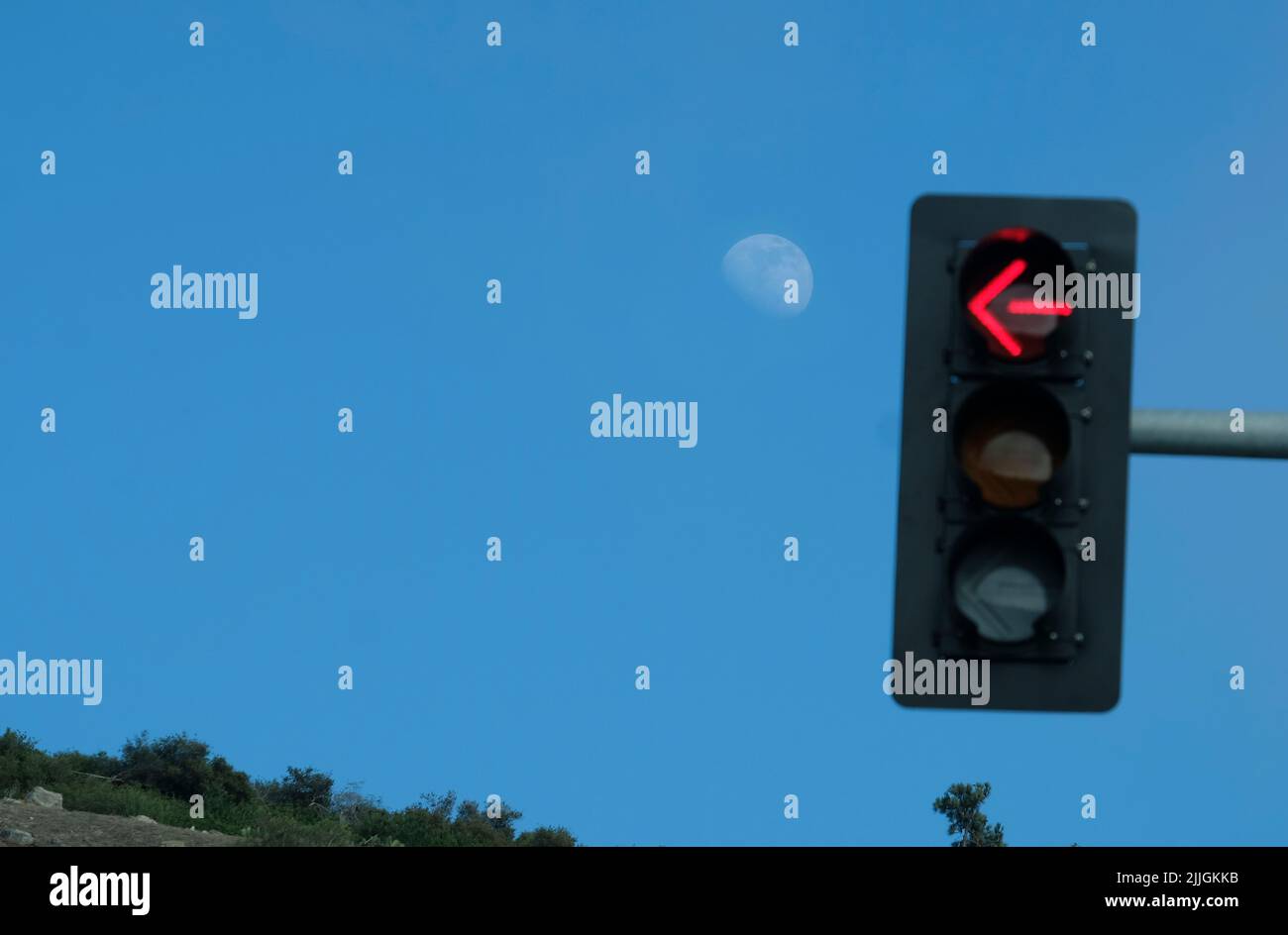 The arrow of a traffic light pointing at the moon with blue sky around ...