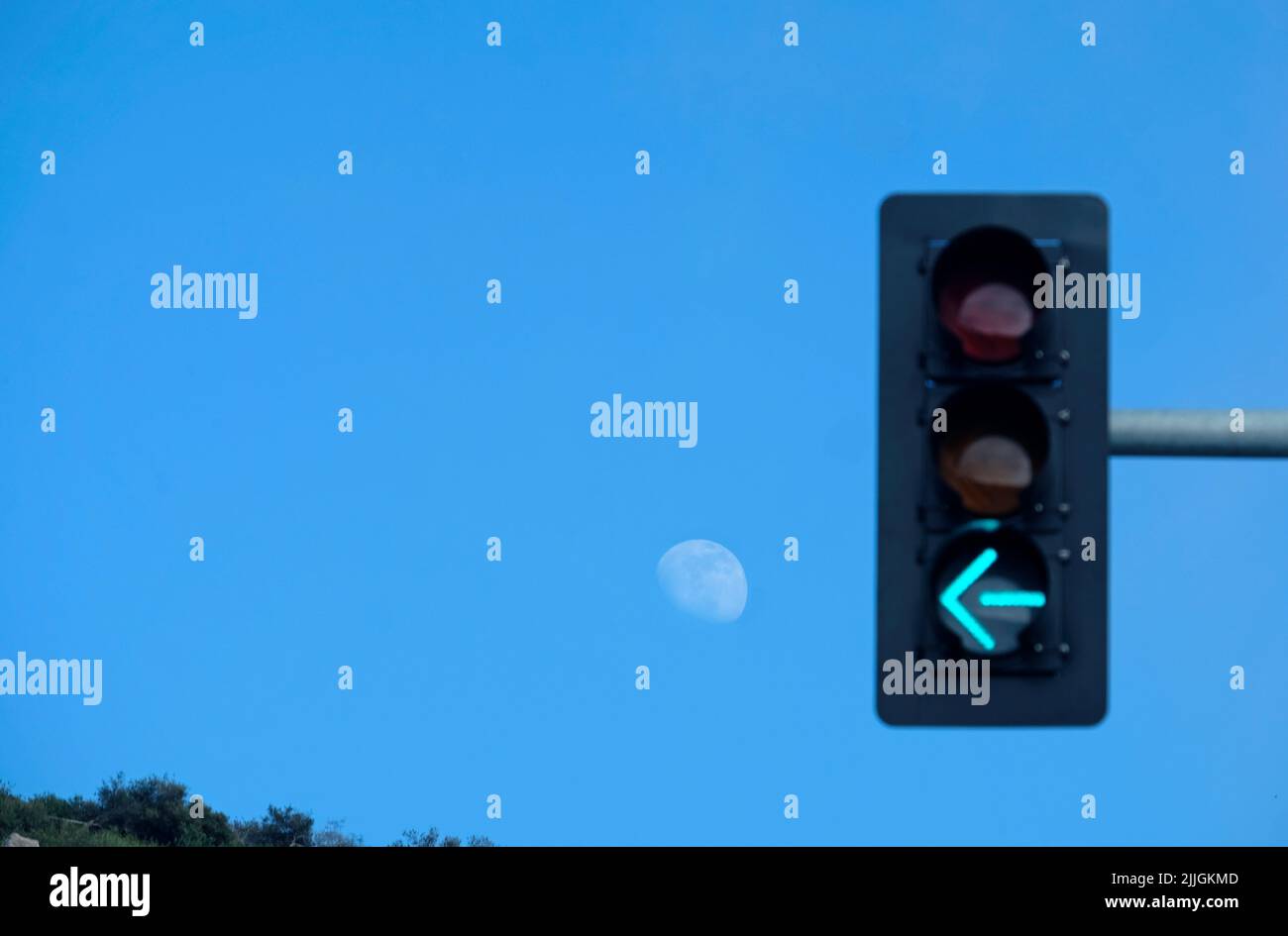 The arrow of a traffic light pointing at the moon with blue sky around ...