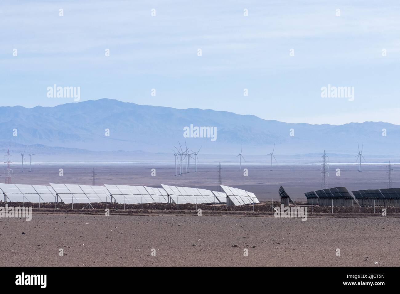 A solar photovoltaic array with wind turbines in the background ...