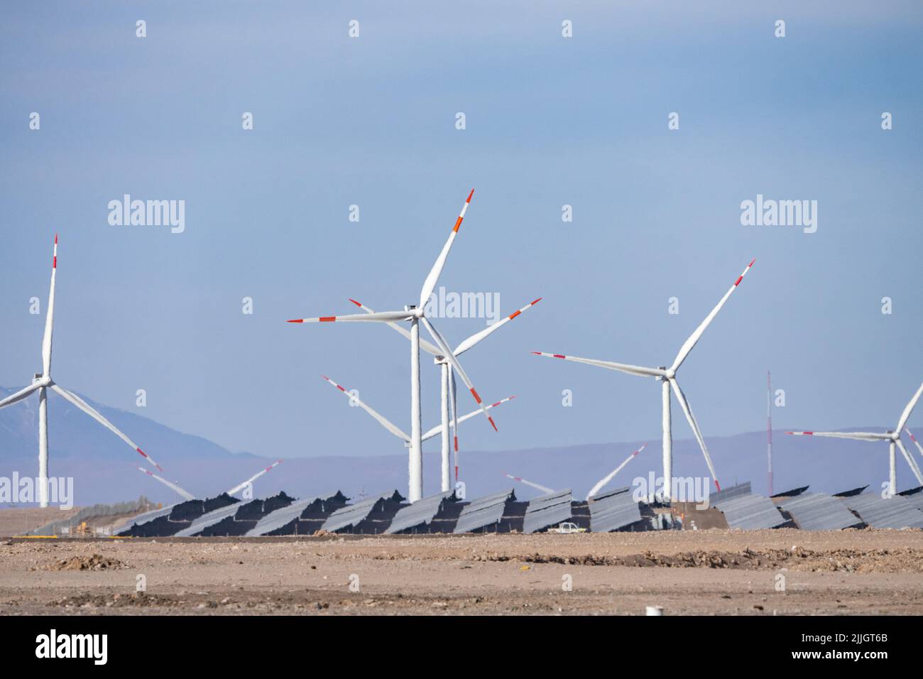 A solar photovoltaic array with wind turbines in the background ...