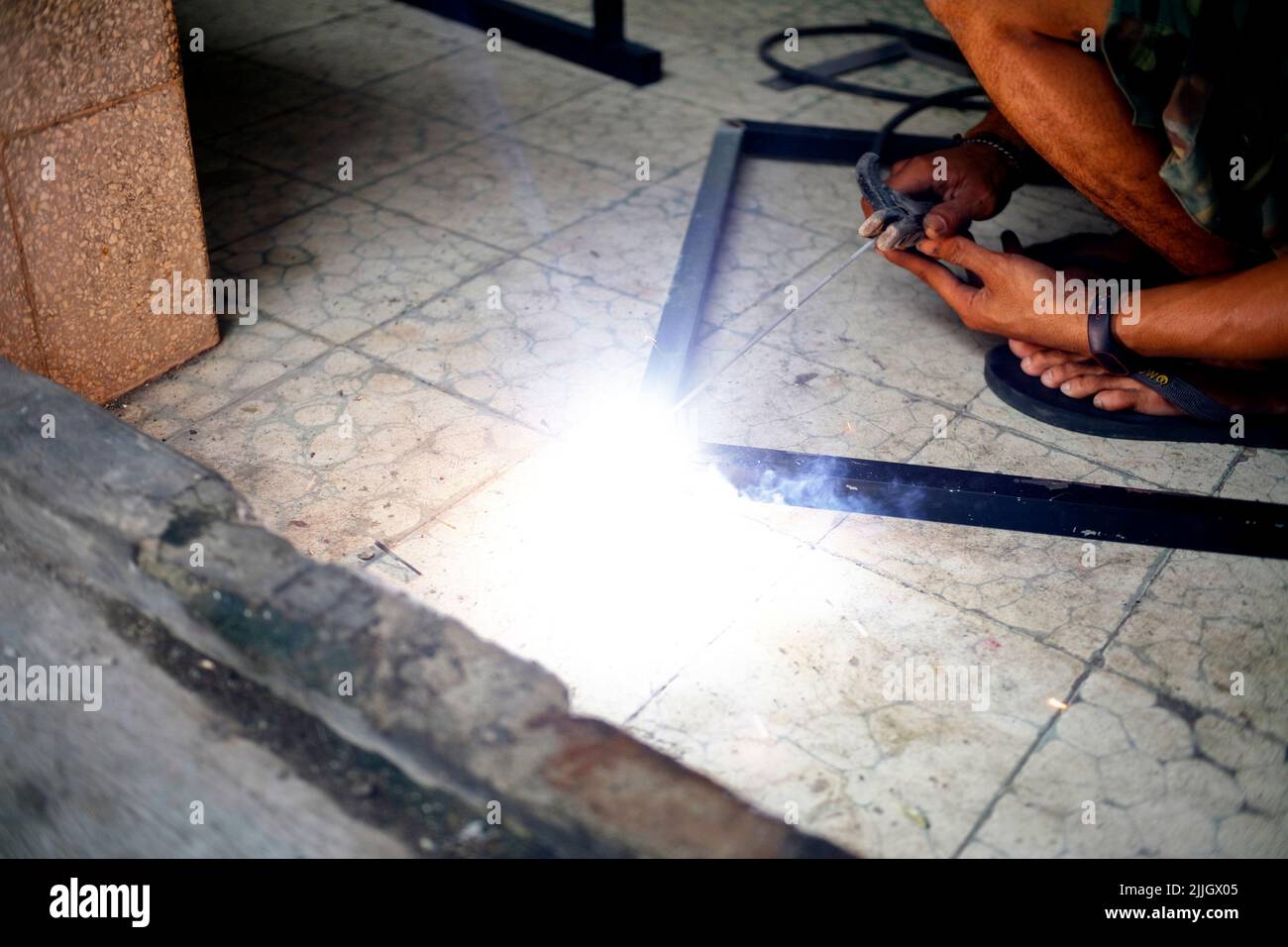 Asian welder holds an iron rack when welding using an electric welder ...