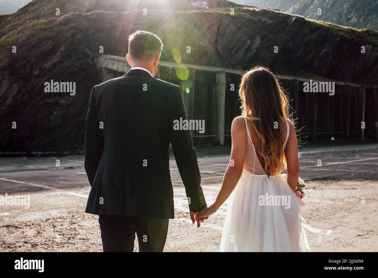 Back view of a wedding bride and groom holding hands walking on the ...