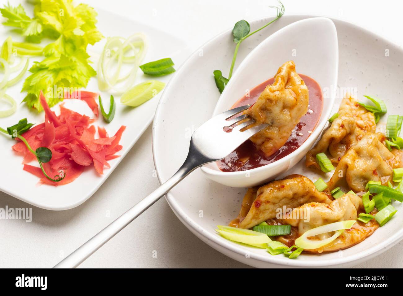 Gyoza fork in bowl with tomato sauce. Gyoza dumplings and chopped leeks ...