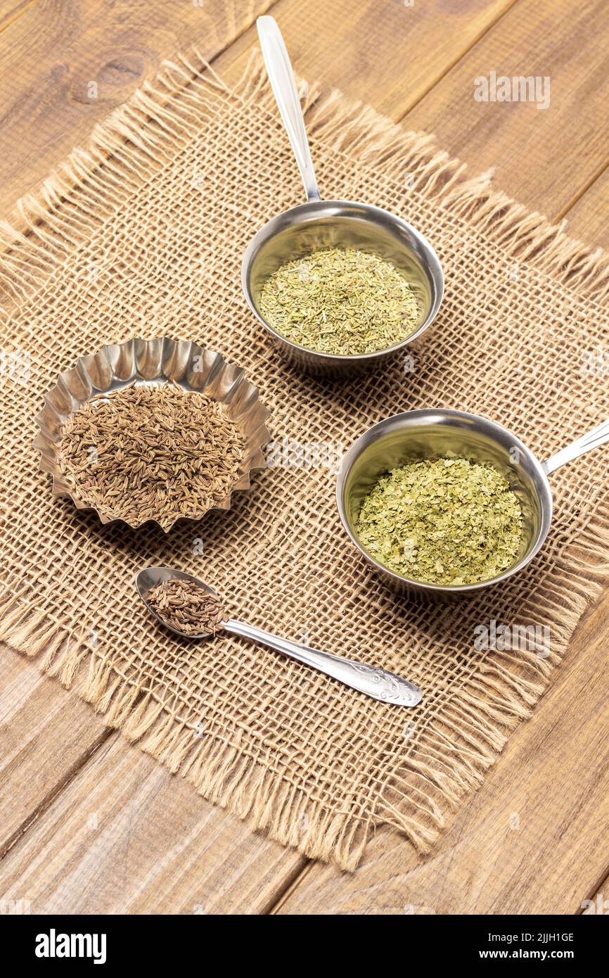 Dry rosemary, cilantro and cumin in spoon in metal bowls on burlap ...