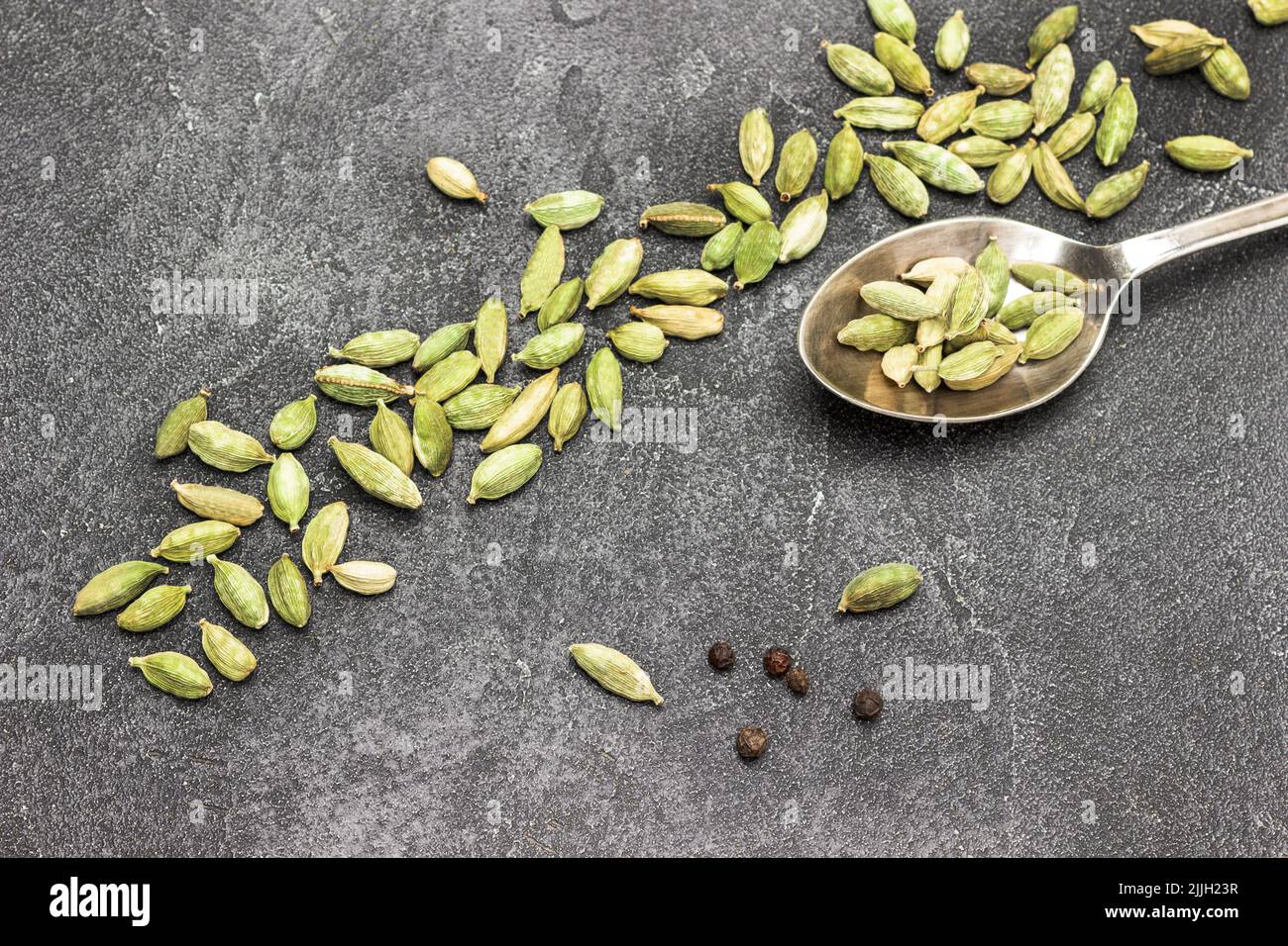 Cardamom seeds in metal spoon and scattered on table. Copy space. Flat ...