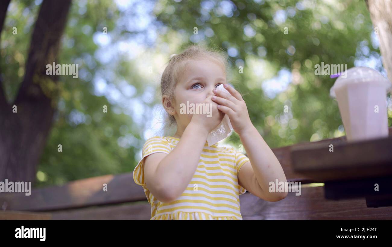 Little girl wipes her face with a paper napkin after eating, there is a ...