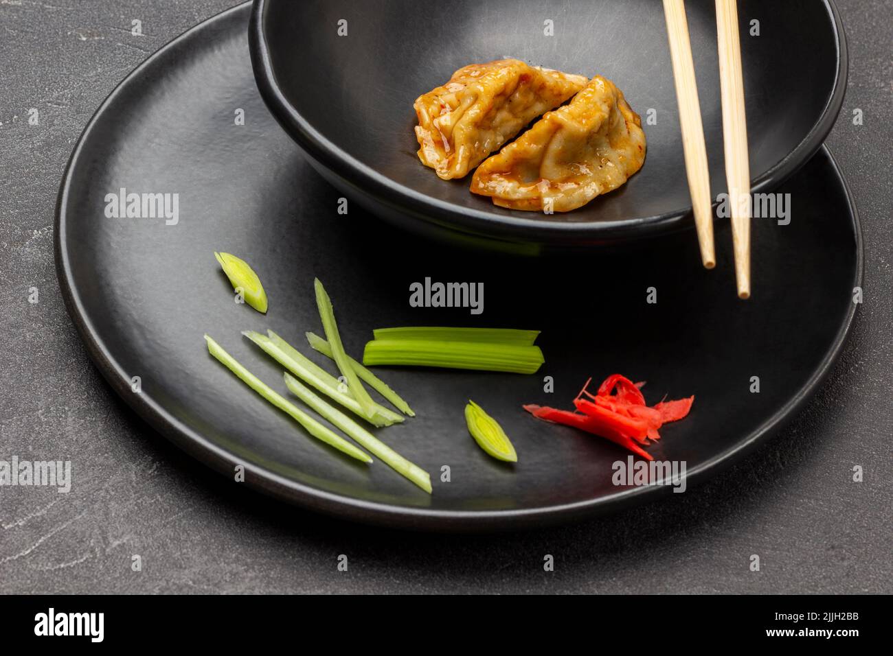 Chopped leek and pickled ginger on black plate. Boiled gyoza dumplings ...