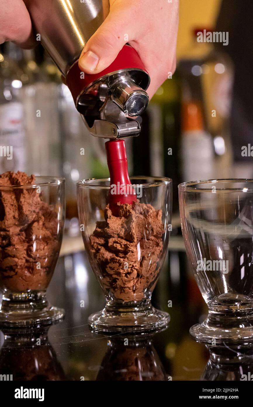 A close up portrait of someone spraying chocolate mousse into glass ...