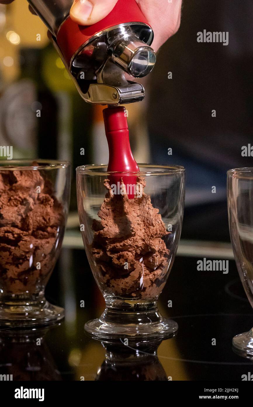 A portrait of someone spraying chocolate mousse into glass cups using ...