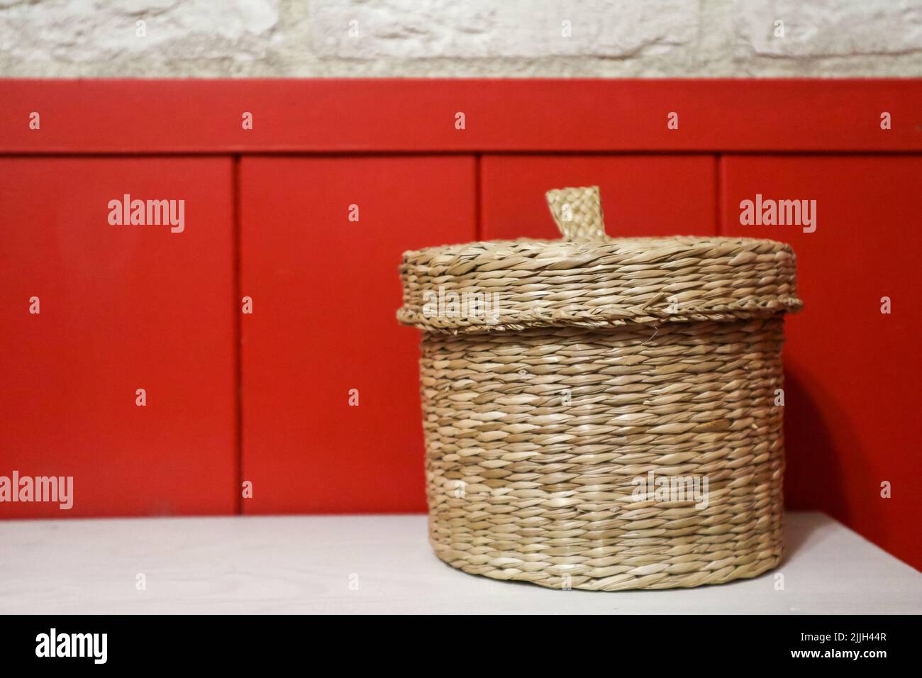 a round wicker container with a lid on a red wall background Stock ...