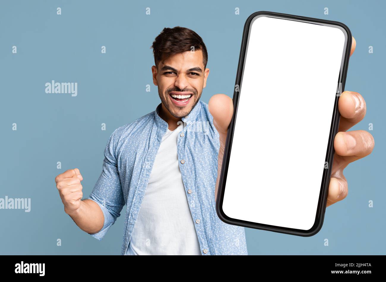 Excited guy shakes clenched fist and showing cell phone, mockup Stock ...