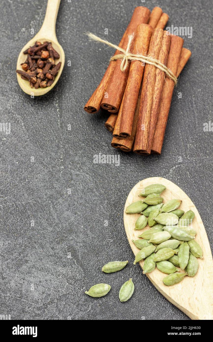 Cardamom in wooden spoon, bunch of cinnamon sticks and cloves in spoon ...