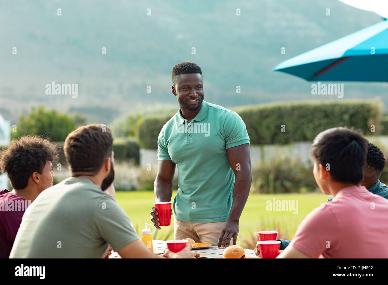 Happy multiracial young man standing and talking with friends while ...