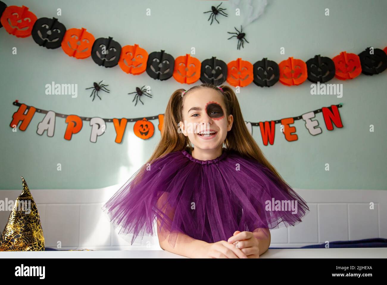 Cute little girl wearing witch hat sitting behind a table in Halloween ...