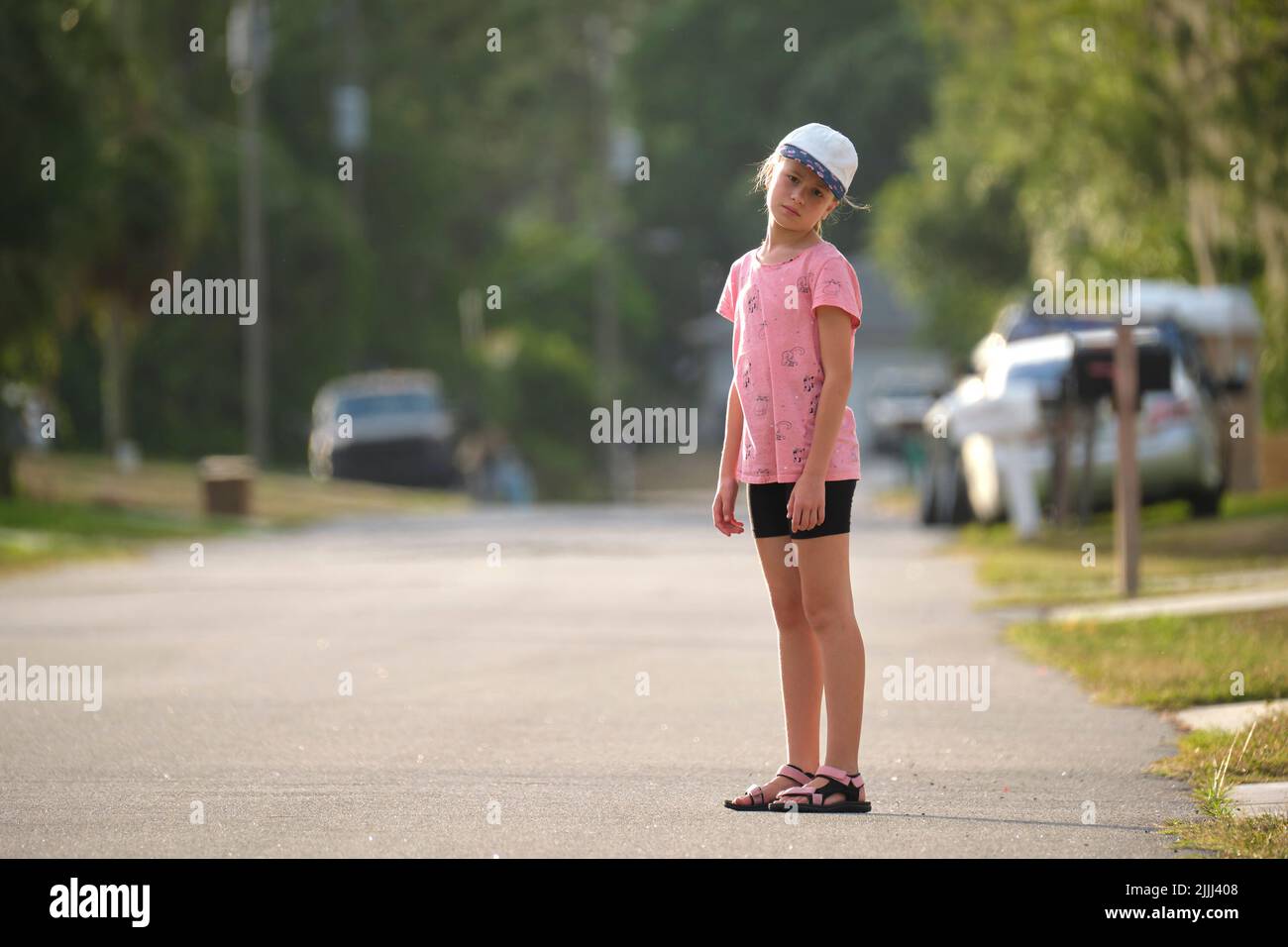 Sad moody tired young child girl standing bored alone looking in camera ...