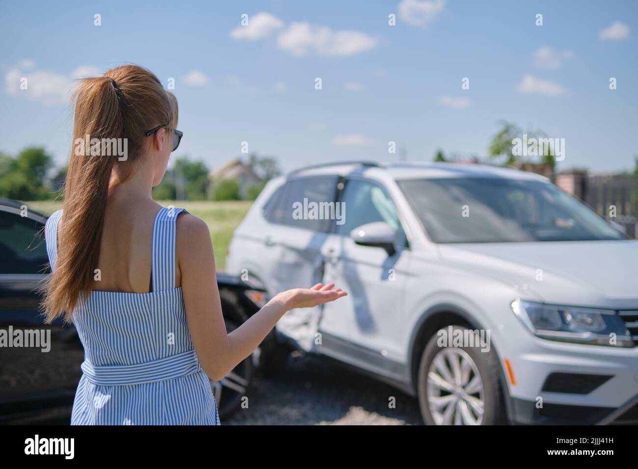 Sad young woman driver standing near her smashed car looking shocked on ...