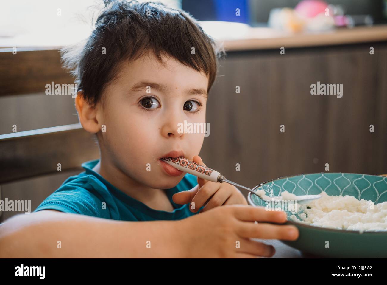 Caucasian child with brown hair eats porridge himself. Healthy ...