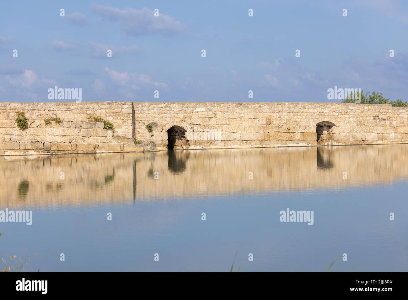An ancient dam reflecting on a lake water under a blue sky Stock Photo ...