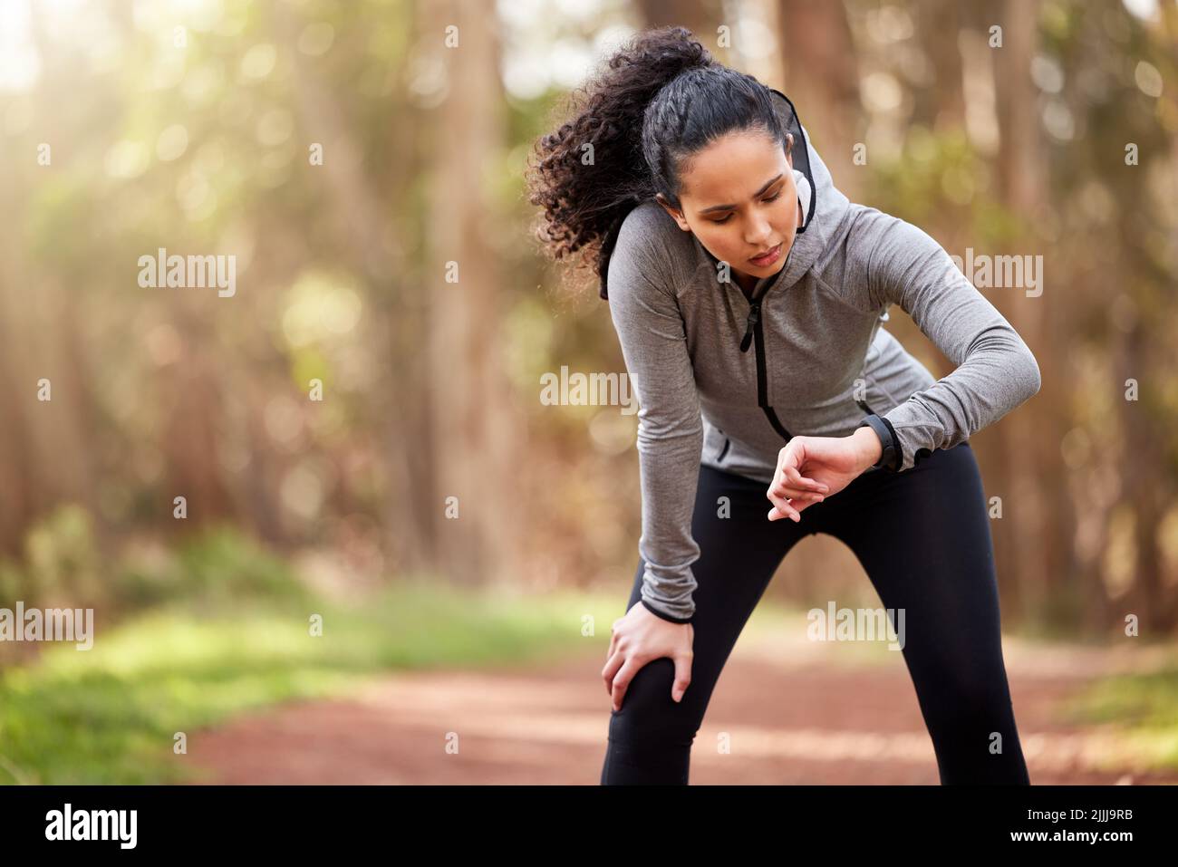 Ive made some progress. a woman checking her watch while out for a run in the woods Stock Photo ...